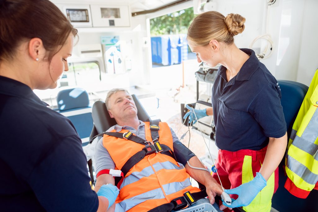 Emergency doctor in ambulance talking to injured man looking che ...